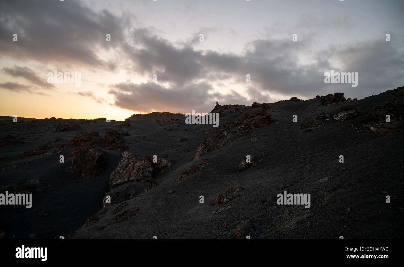 landscape with volcanic sand and molten lava rocks in a sunset with ...