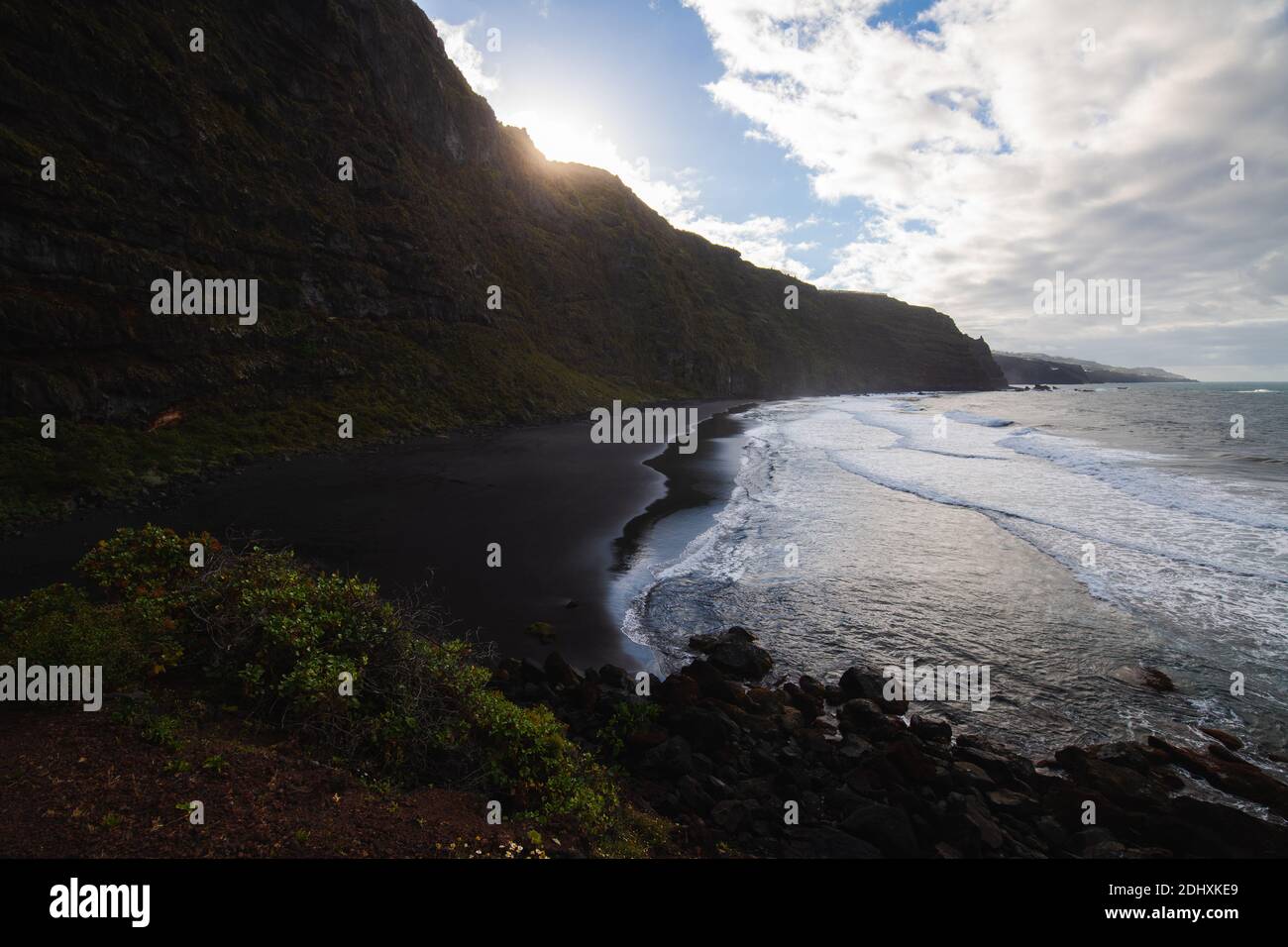 volcanic sand beach and cliffs with a lot of green vegetation during a ...