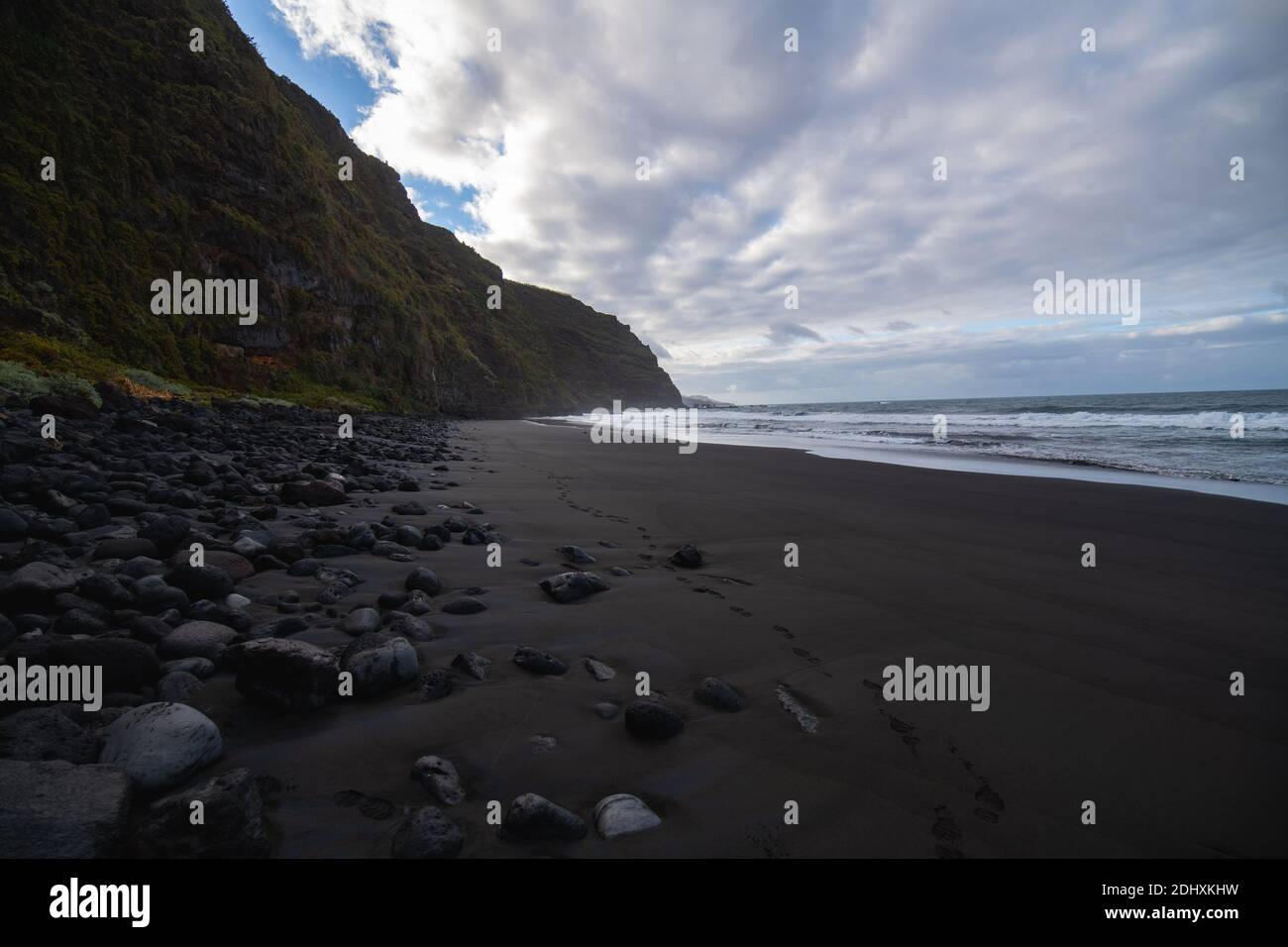 volcanic sand beach with polished rocks on a cliff with green ...