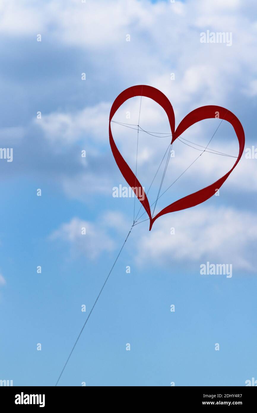 Red kite in the shape of heart in the blue sky with clouds at the ...