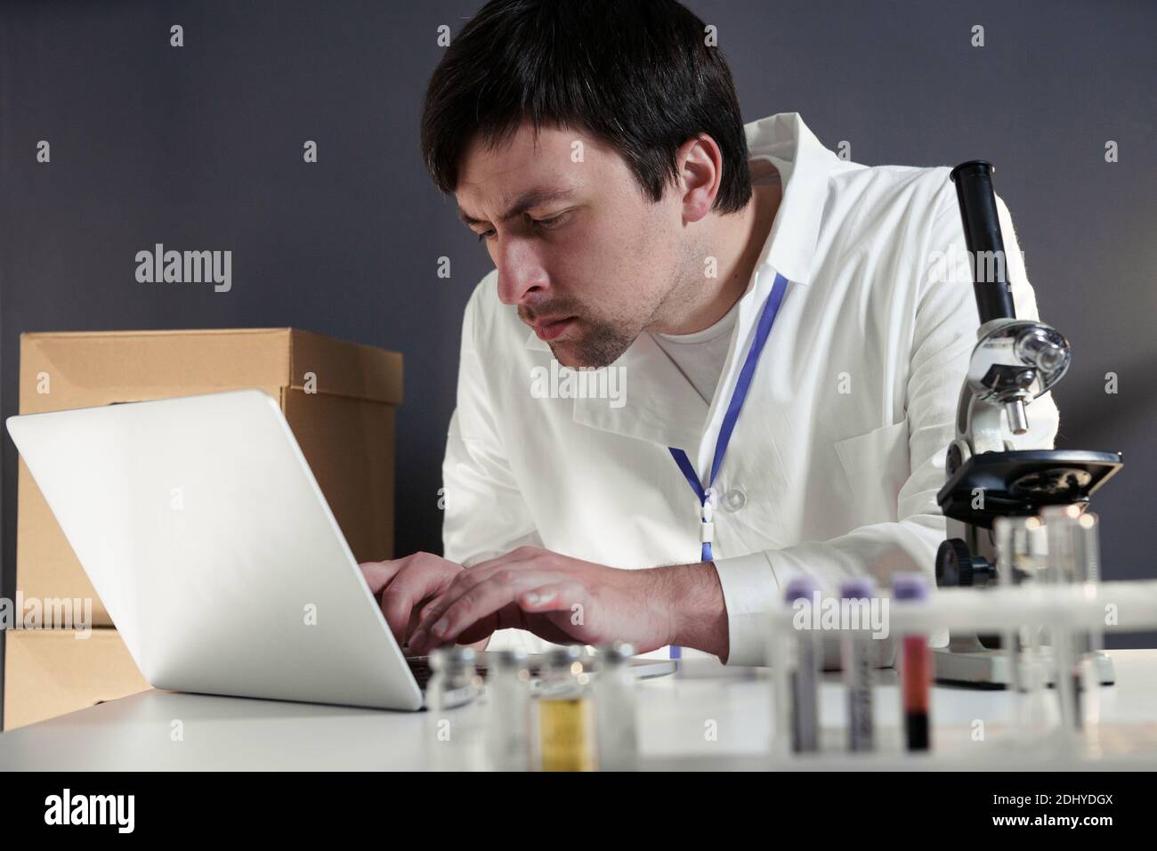 Scientist in lab coat and eyeglasses working at workplace with laptop ...
