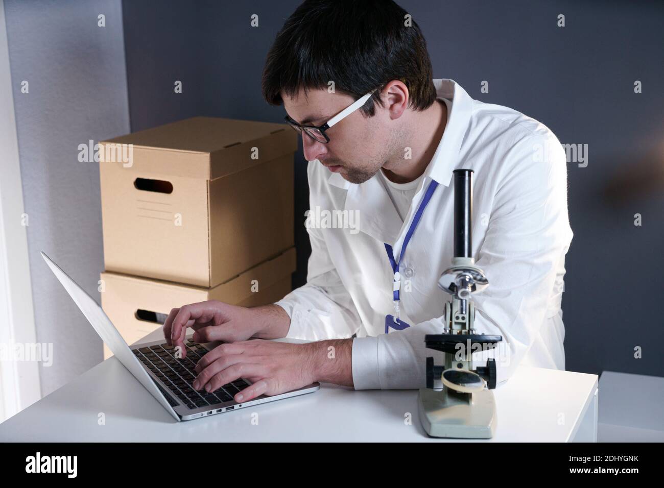 Scientist in lab coat and eyeglasses working at workplace with laptop ...