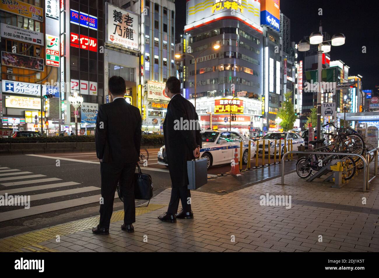 Men in suits wait on a red light looking towards Kabukicho in Shinjuku ...