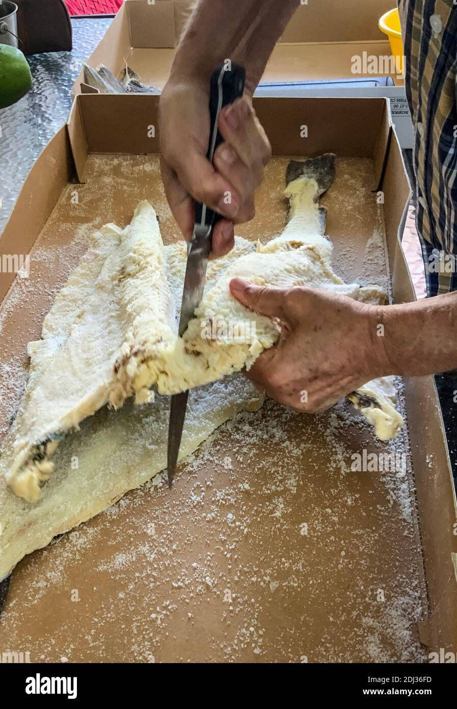 Dried and salted cod fish being cut into portions by a man with a large ...