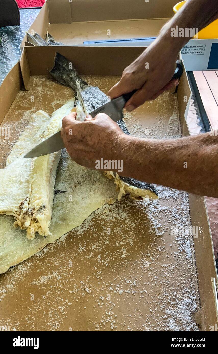 Dried and salted cod fish being cut into portions by a man with a large ...