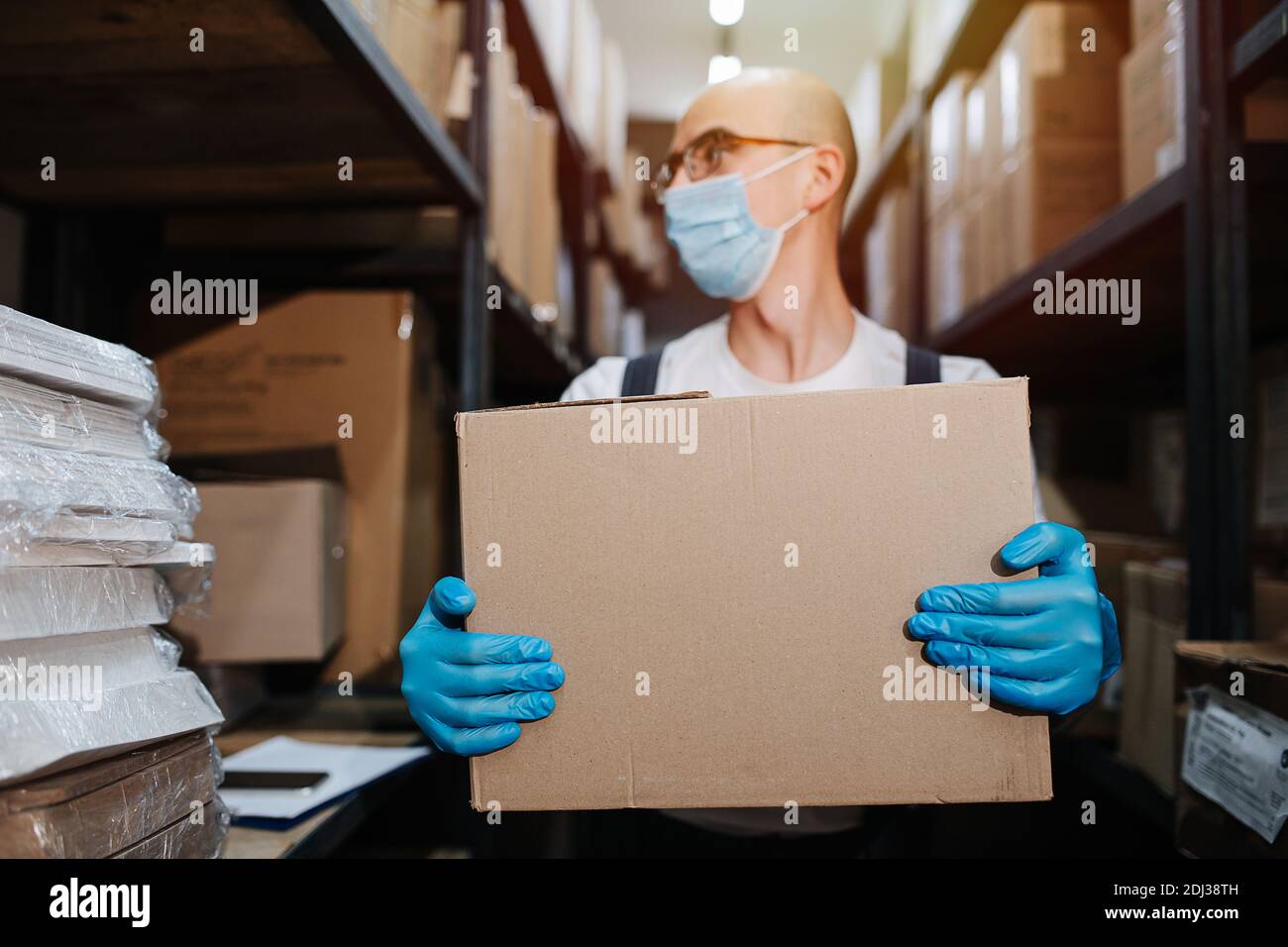 Tired warehouse worker carrying box, wearing mask and gloves. Selective ...