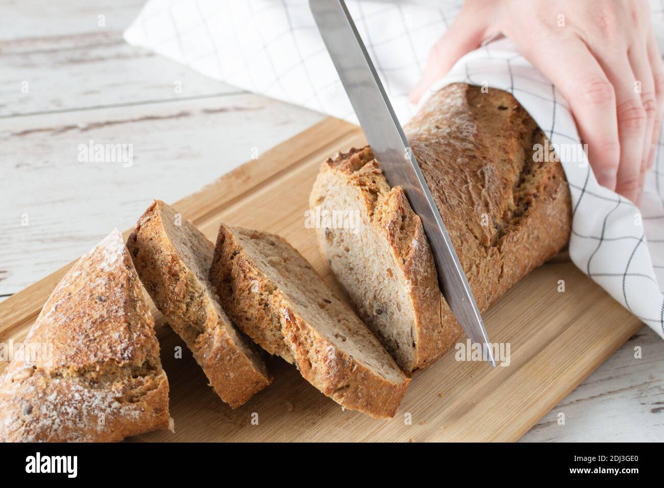 Woman hand cutting loaf of bread on white wooden table. Loaf of ...