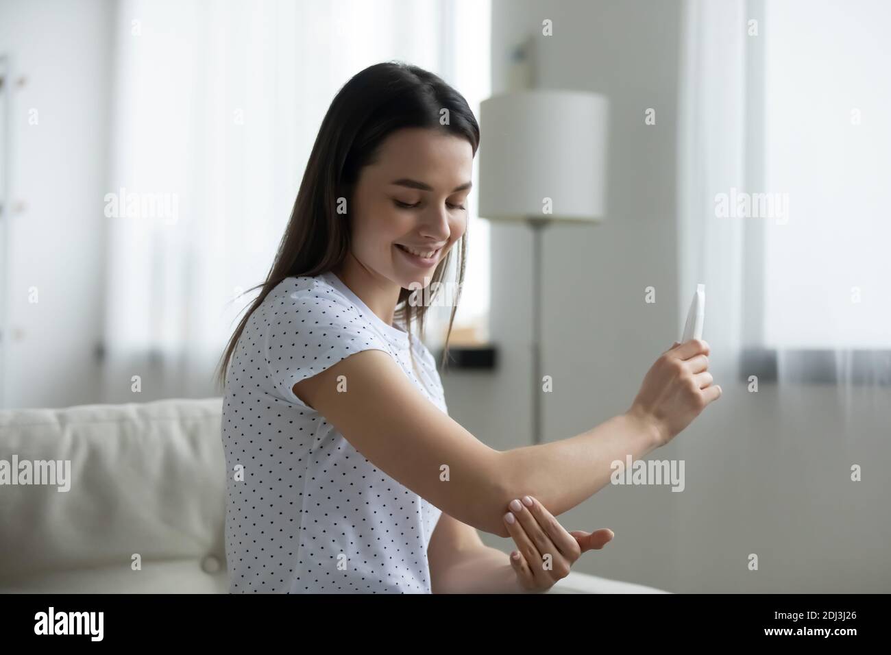 Smiling beautiful young woman applying moisturizing cream on elbow ...