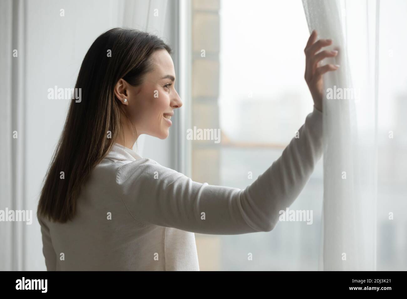 Close up happy young woman opening curtains, looking out window Stock ...