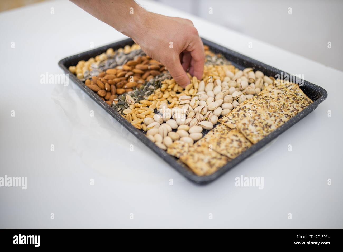 Male hand picking nuts from a black tray with seeds and nuts Stock ...