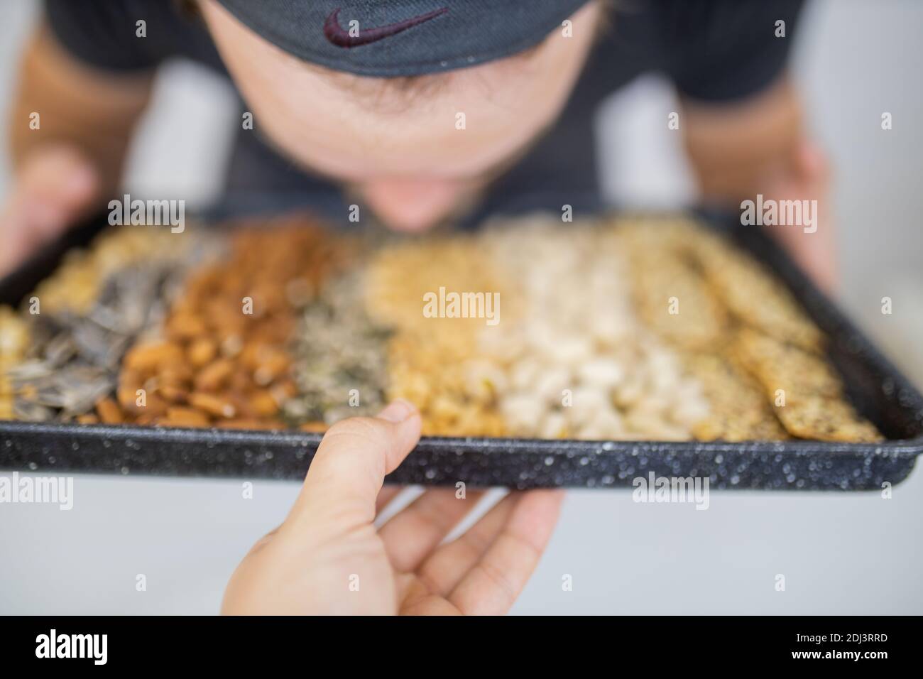 Man holding and smelling a black tray of nuts and seeds Stock Photo - Alamy