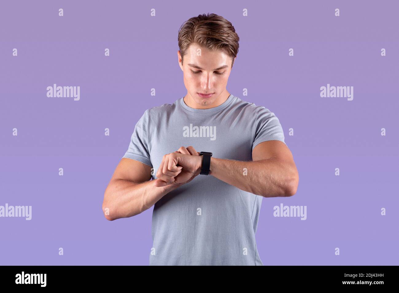 Strong athletic man looking at his smartwatch on violet studio ...