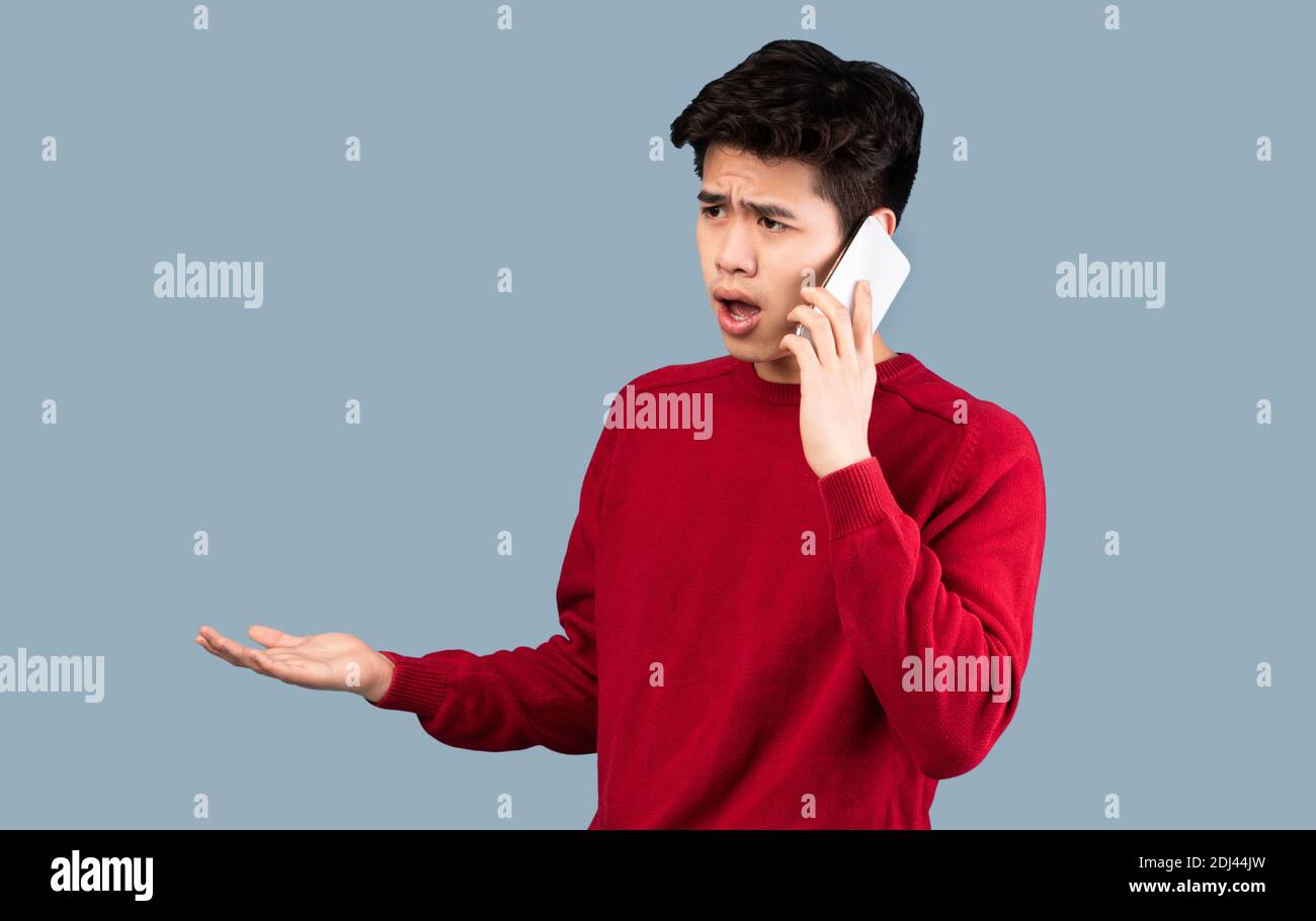 Confused asian man talking on smartphone at studio Stock Photo - Alamy