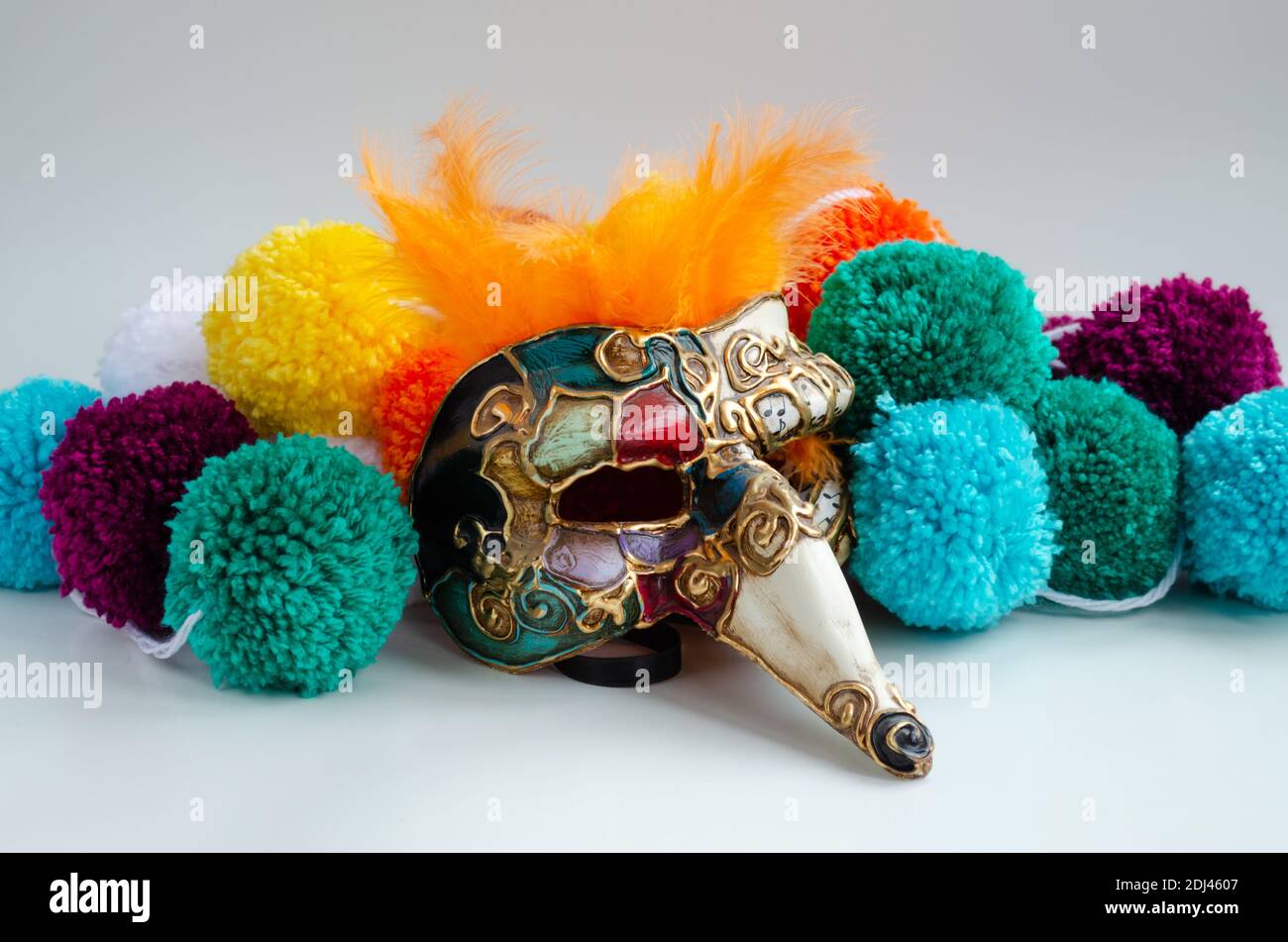 A carnival mask with yellow feathers and colorful wool pom poms ...