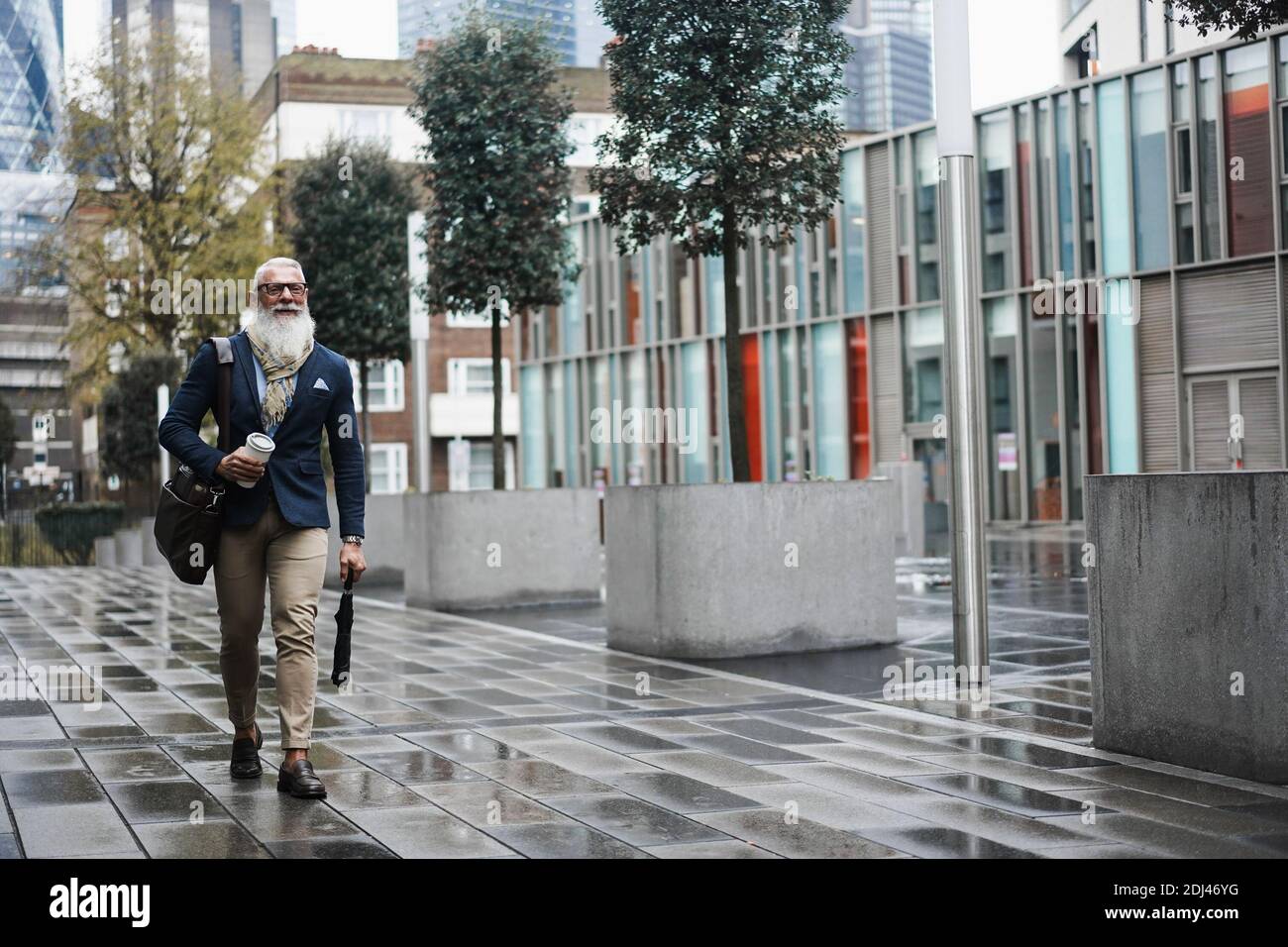 Happy business senior man walking to work on rainy winter day - Focus ...