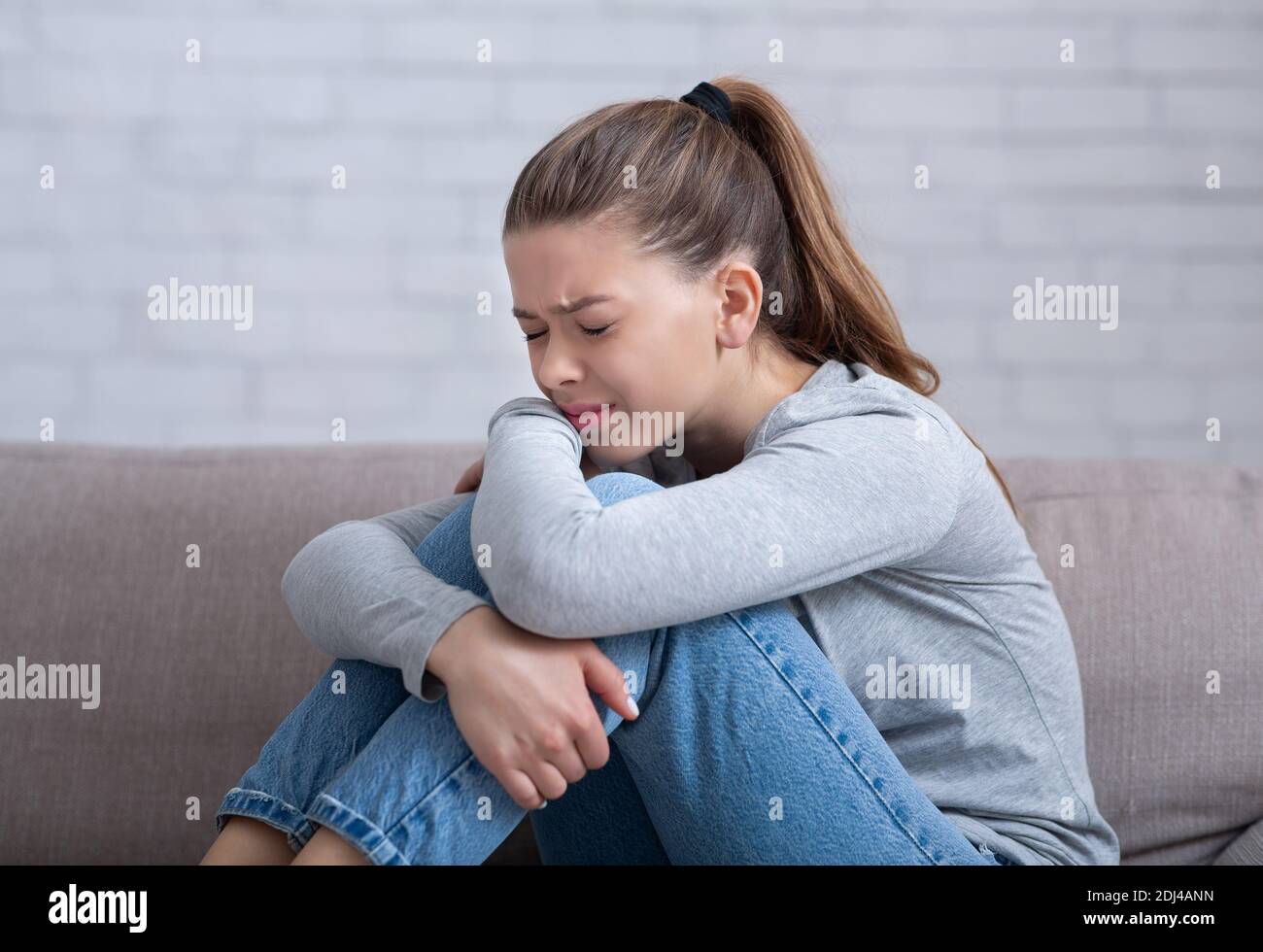 Millennial lady with depression sitting on sofa at home, closing her ...