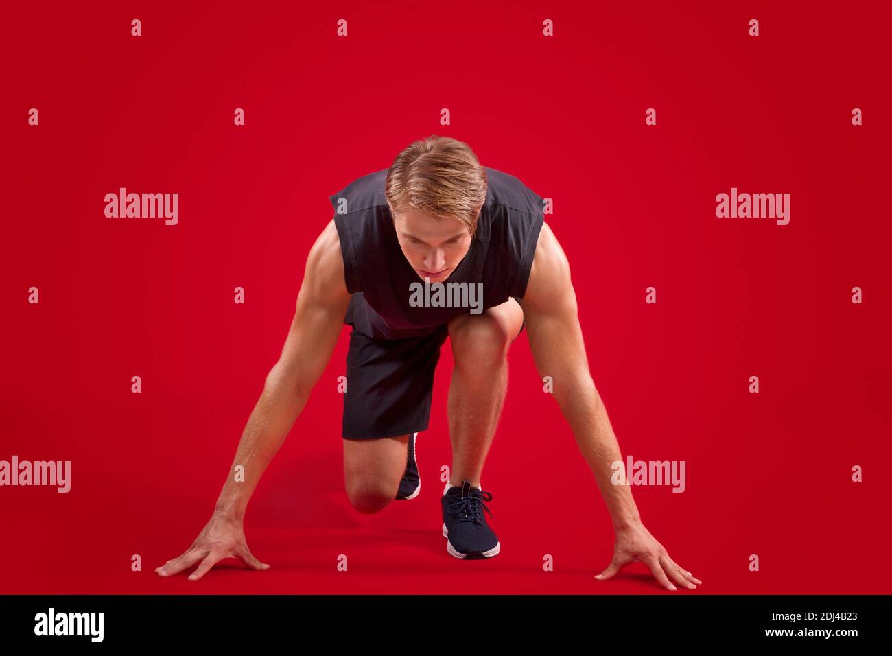 Motivated young sportsman standing on start, ready to run race over red ...