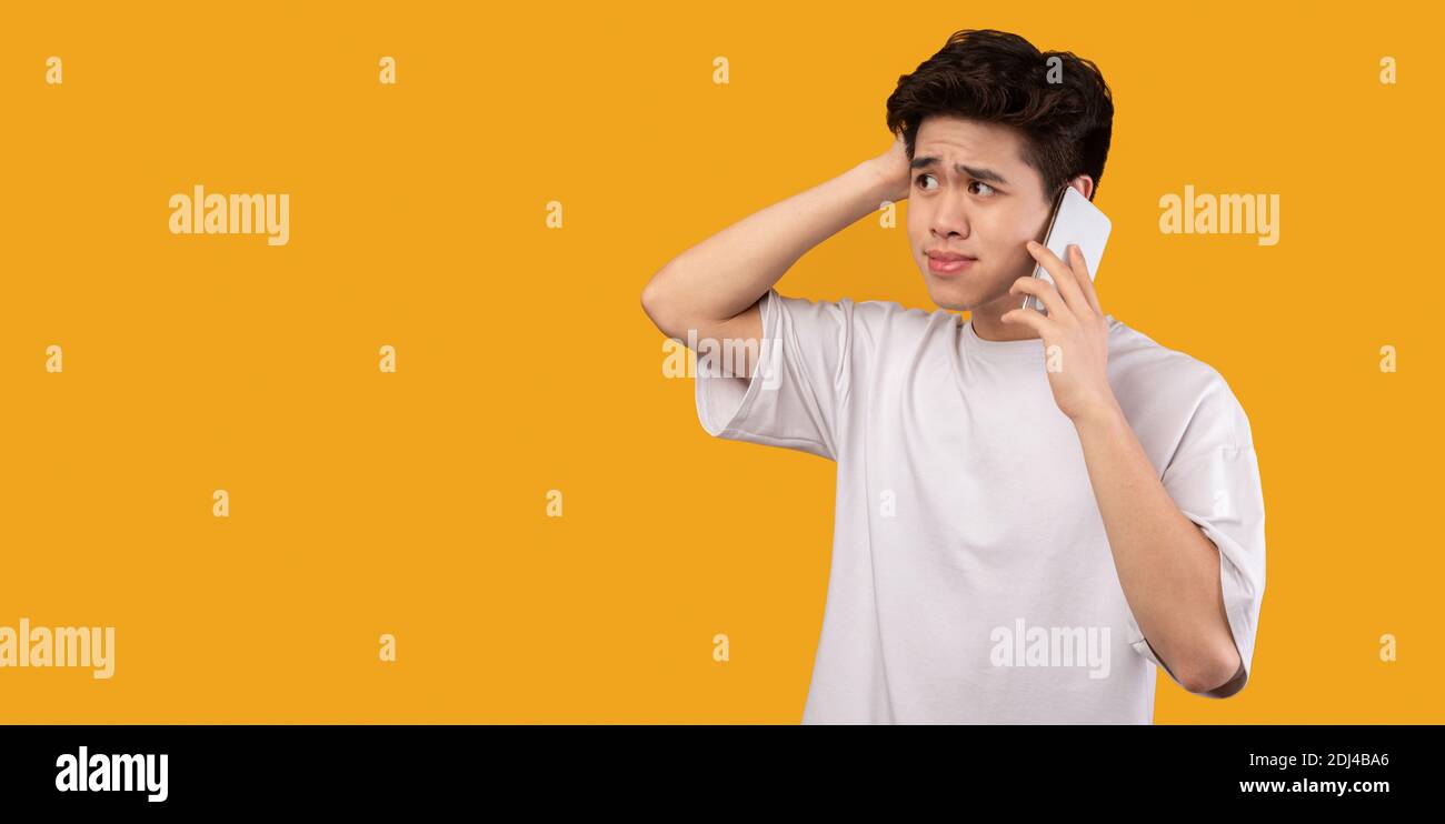 Confused asian man talking on mobile phone at studio Stock Photo - Alamy