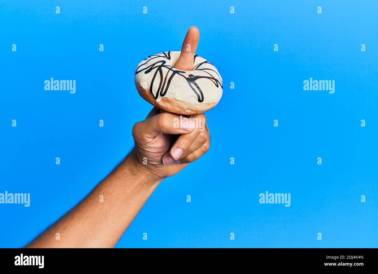 Finger of hispanic man holding donut over isolated blue background ...