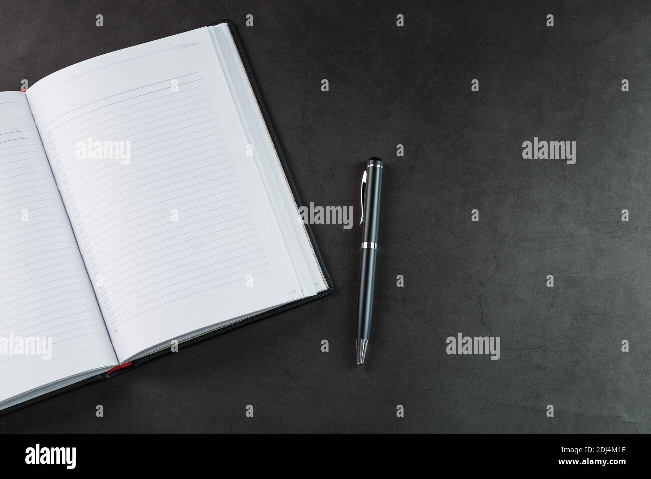 Office desk with black notepad and pen on black background. Top view ...