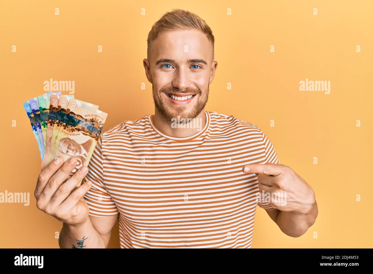 Young caucasian man holding canadian dollars smiling happy pointing ...