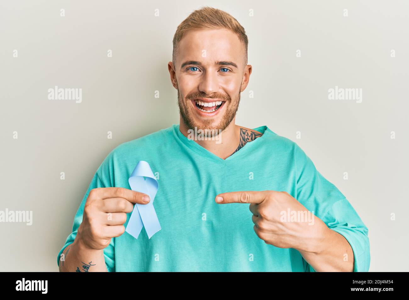 Young caucasian man holding blue ribbon smiling happy pointing with ...
