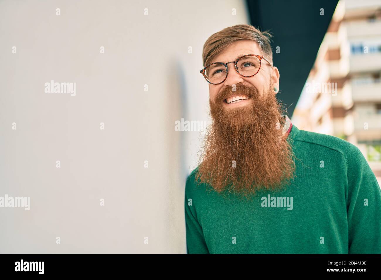 Young irish man with redhead beard smiling happy leaning on the wall at ...