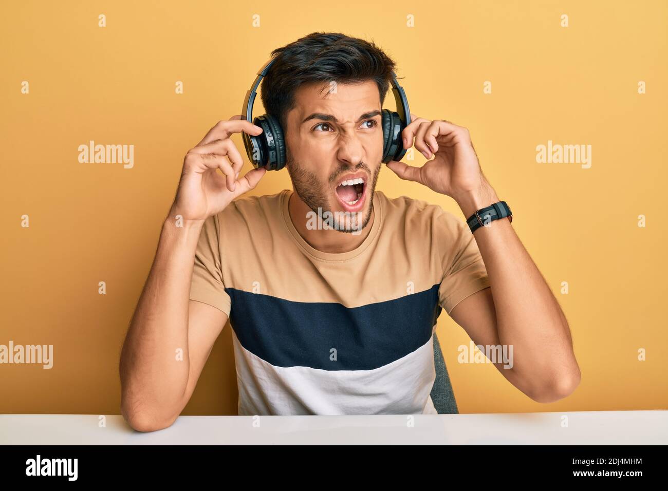 Young handsome man listening to music wearing headphones angry and mad ...