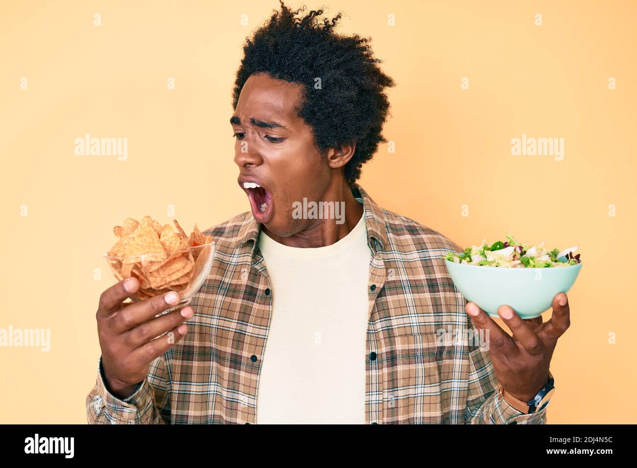 Handsome african american man with afro hair holding nachos and healthy ...