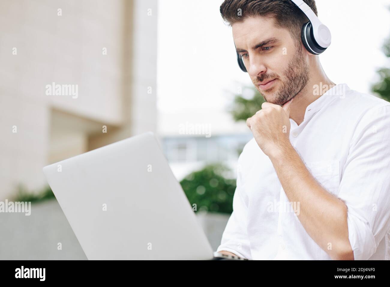 Pensive handsome young software developer in headphones rubbing chin ...