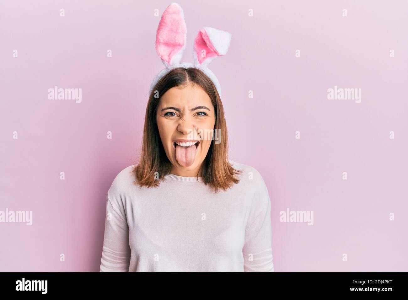 Young beautiful woman wearing cute easter bunny ears sticking tongue ...