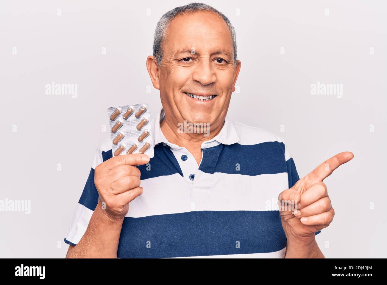 Senior man with grey hair holding pills smiling happy pointing with ...