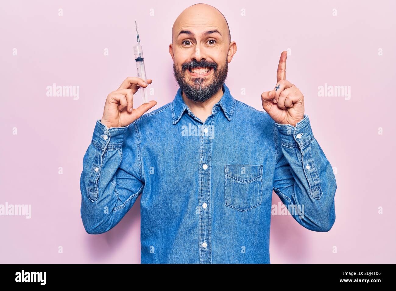 Young handsome man holding syringe surprised with an idea or question pointing finger with happy ...
