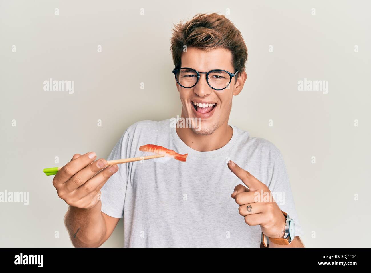 Handsome caucasian man eating prawn sushi using chopsticks smiling ...