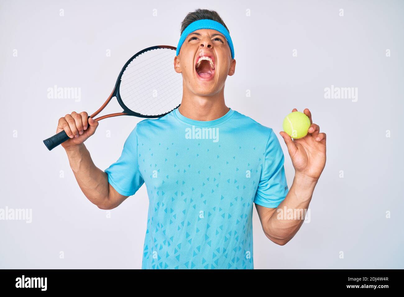 Young hispanic boy playing tennis holding racket and ball angry and mad ...