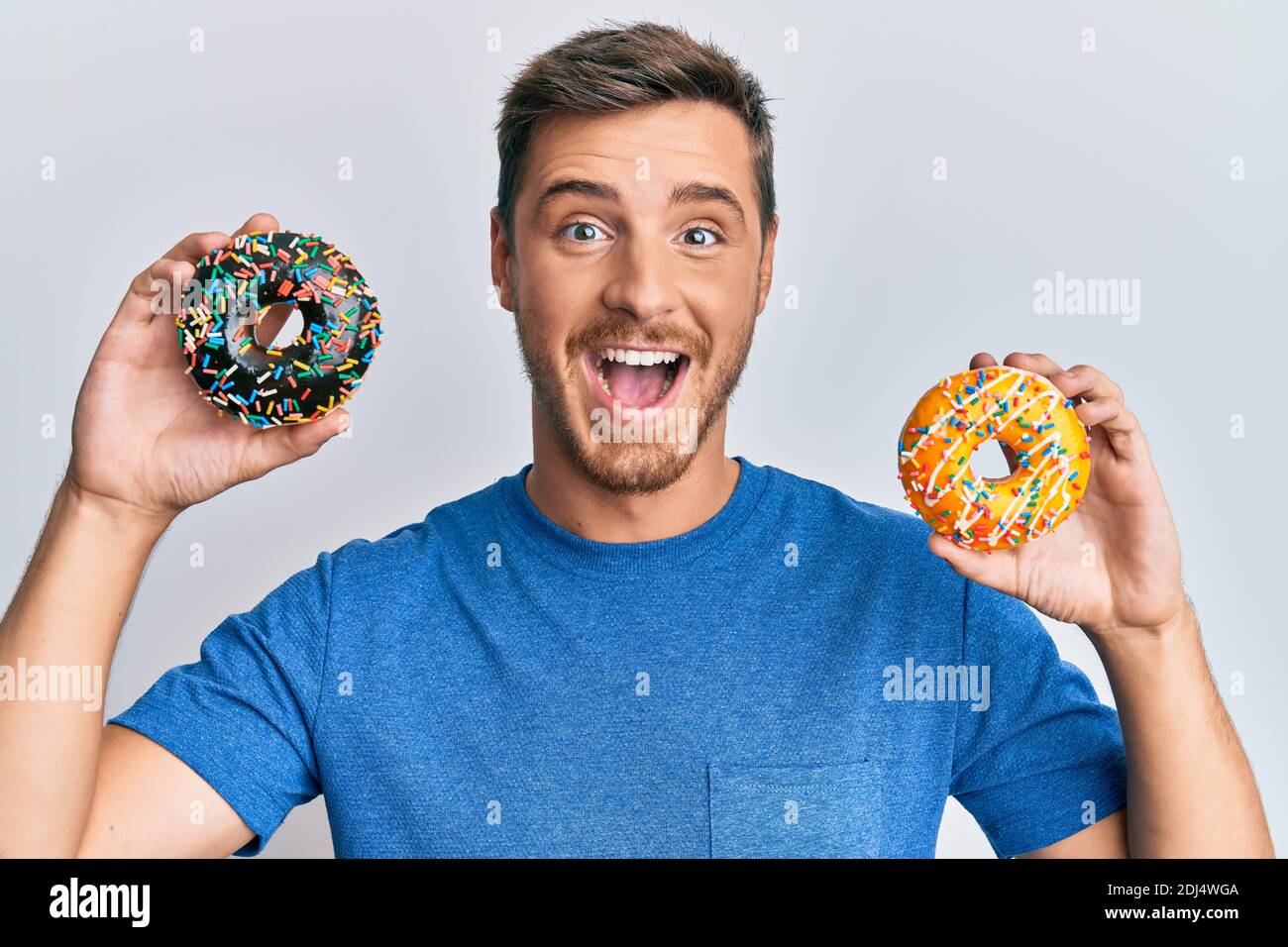 Handsome caucasian man holding tasty colorful doughnuts celebrating ...