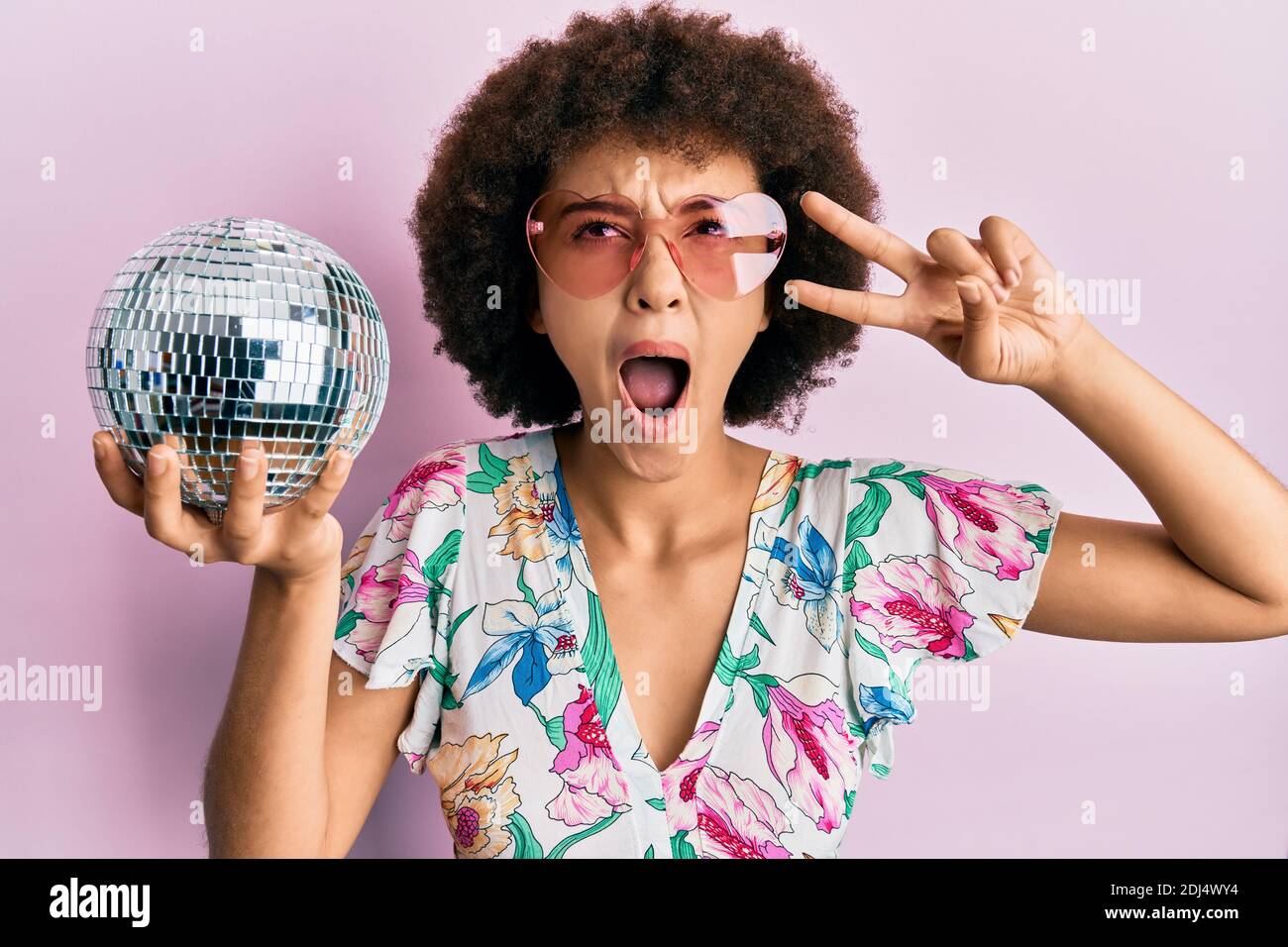 Young hispanic girl wearing summer style holding disco ball angry and ...