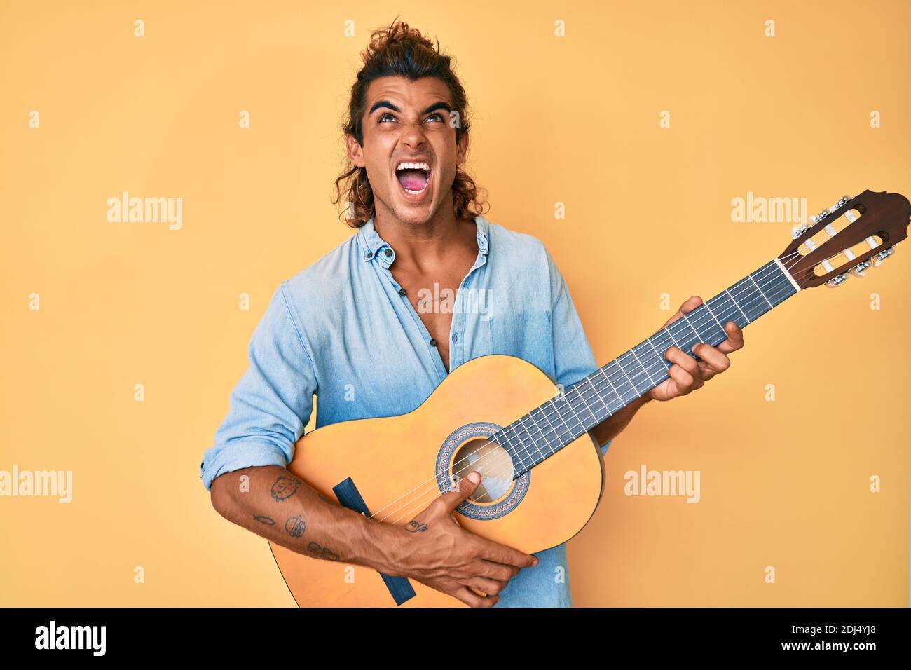 Young hispanic man playing classical guitar angry and mad screaming ...