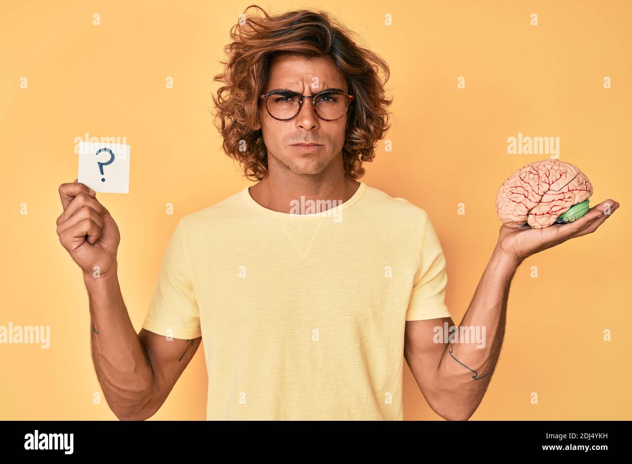 Young hispanic man holding brain and question mark skeptic and nervous ...