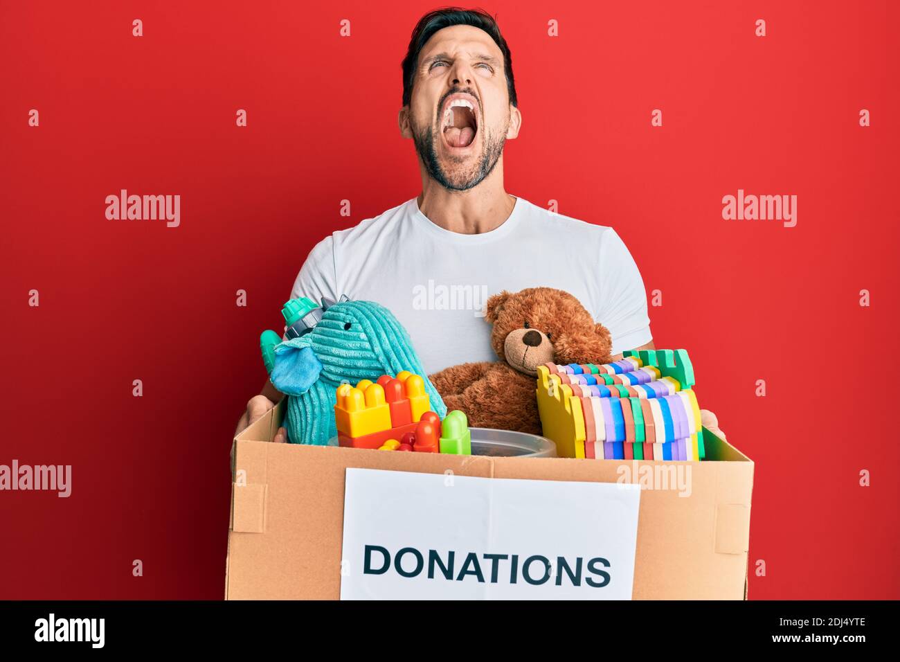 Young handsome man holding donation box with toys angry and mad ...