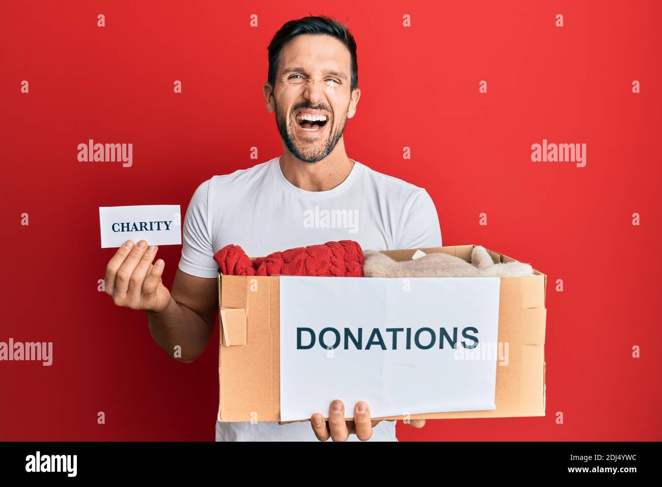 Young handsome man volunteer holding donations box with clothes smiling ...