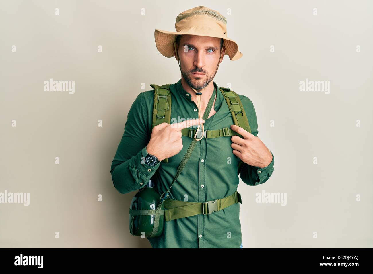 Handsome man with beard wearing explorer hat and backpack pointing with ...
