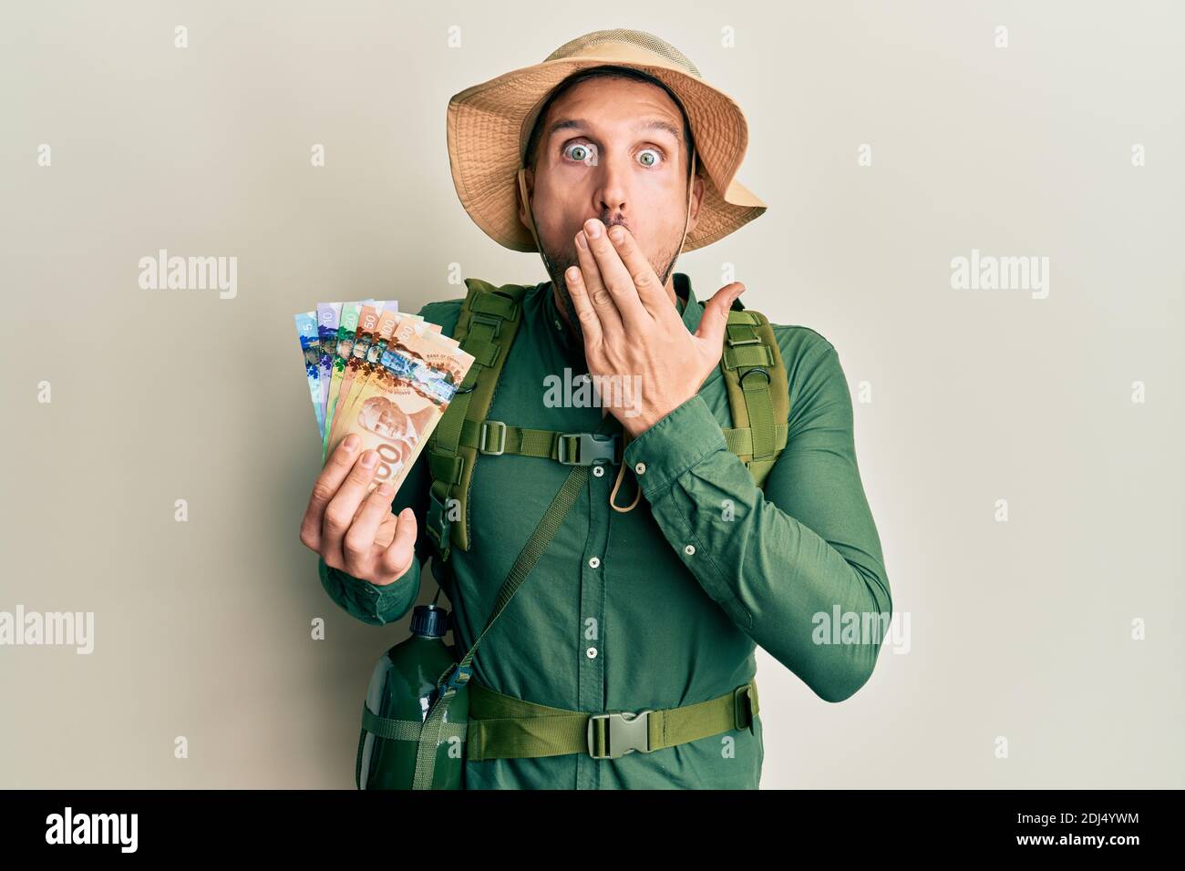 Handsome man with beard wearing explorer hat holding canadian dollars ...