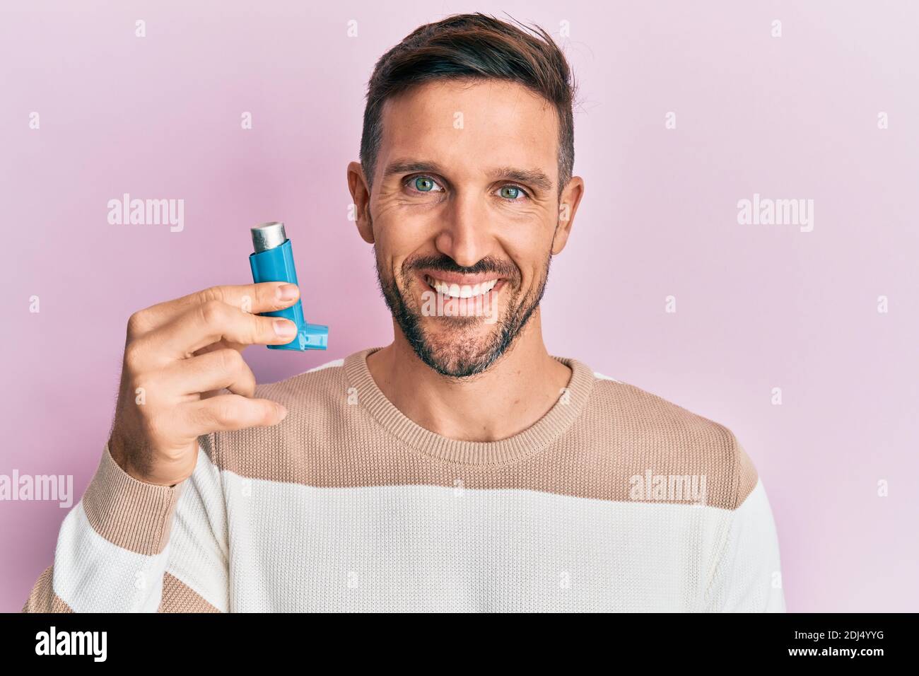 Handsome man with beard holding medical asthma inhaler looking positive ...