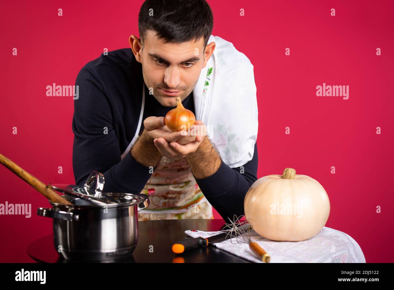 Male chef with apron in a kitchen holds a bow and examines it. Pink ...