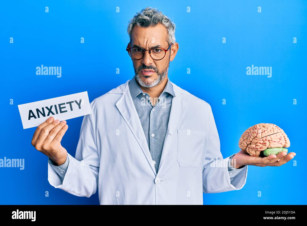 Middle age grey-haired man wearing doctor coat holding brain and ...
