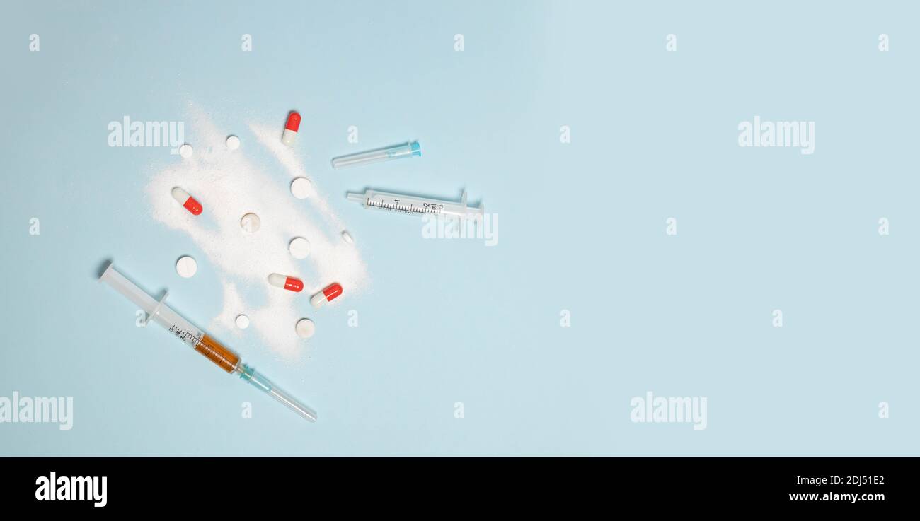 White pills, colored capsules and syringes with a needle on a light ...