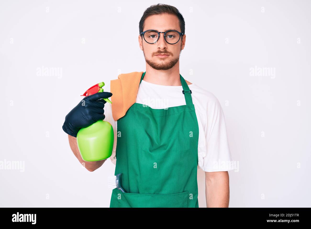Young handsome man wearing apron holding sprayer thinking attitude and ...