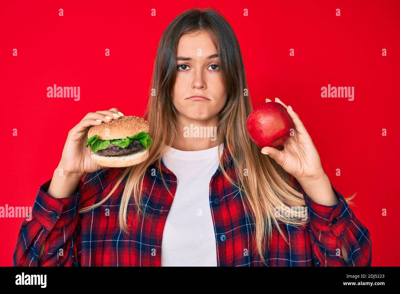 Beautiful caucasian woman comparing burger and healthy red apple ...