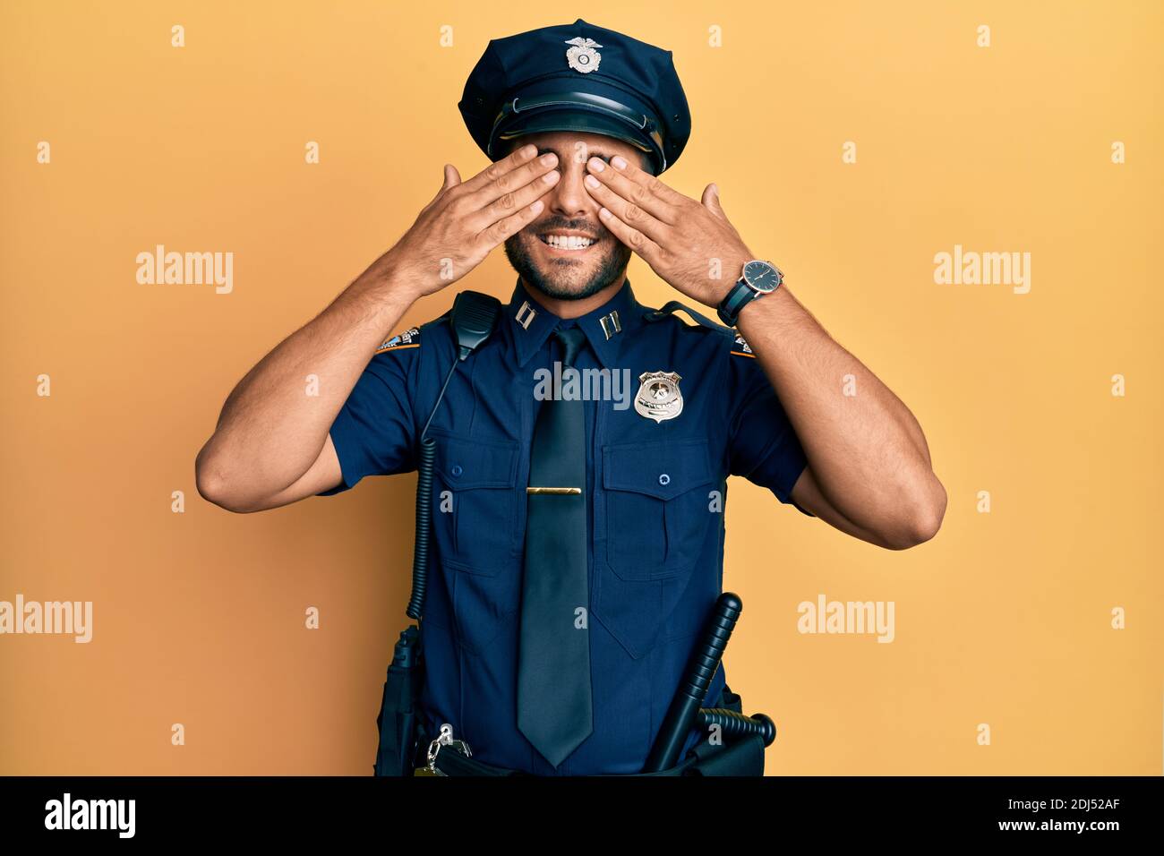 Handsome hispanic man wearing police uniform covering eyes with hands ...